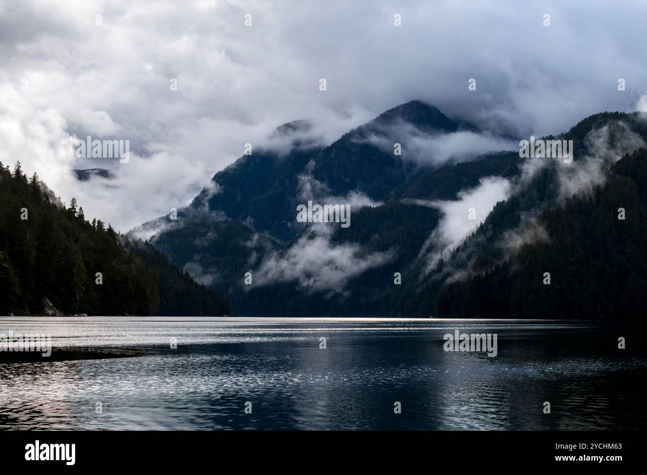 Misty clouds of a clearing rain storm move past dark forested mountains ...