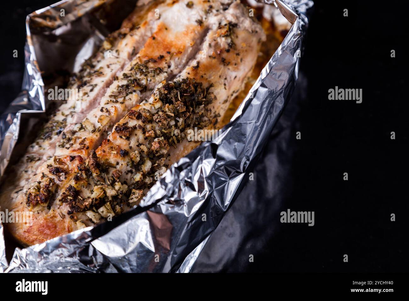 Baked meat with seasoning in foil on black tray Stock Photo - Alamy