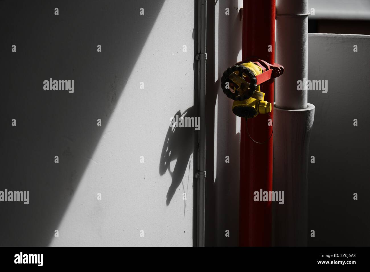 Red fire hydrant pipe with yellow valve in a corner of a building ...