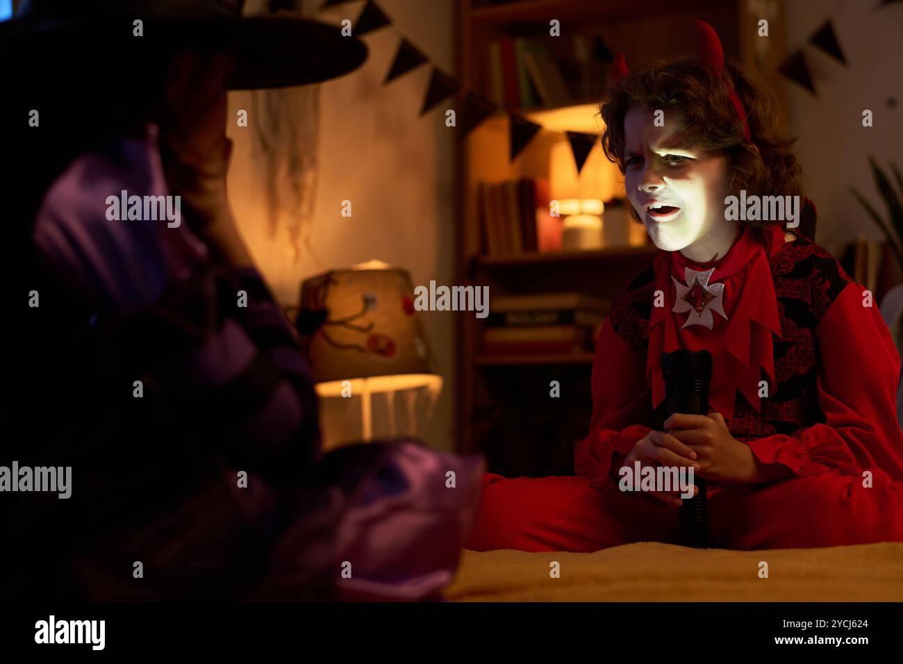 Spooky boy in costume of demon frightening his sister with horror ...