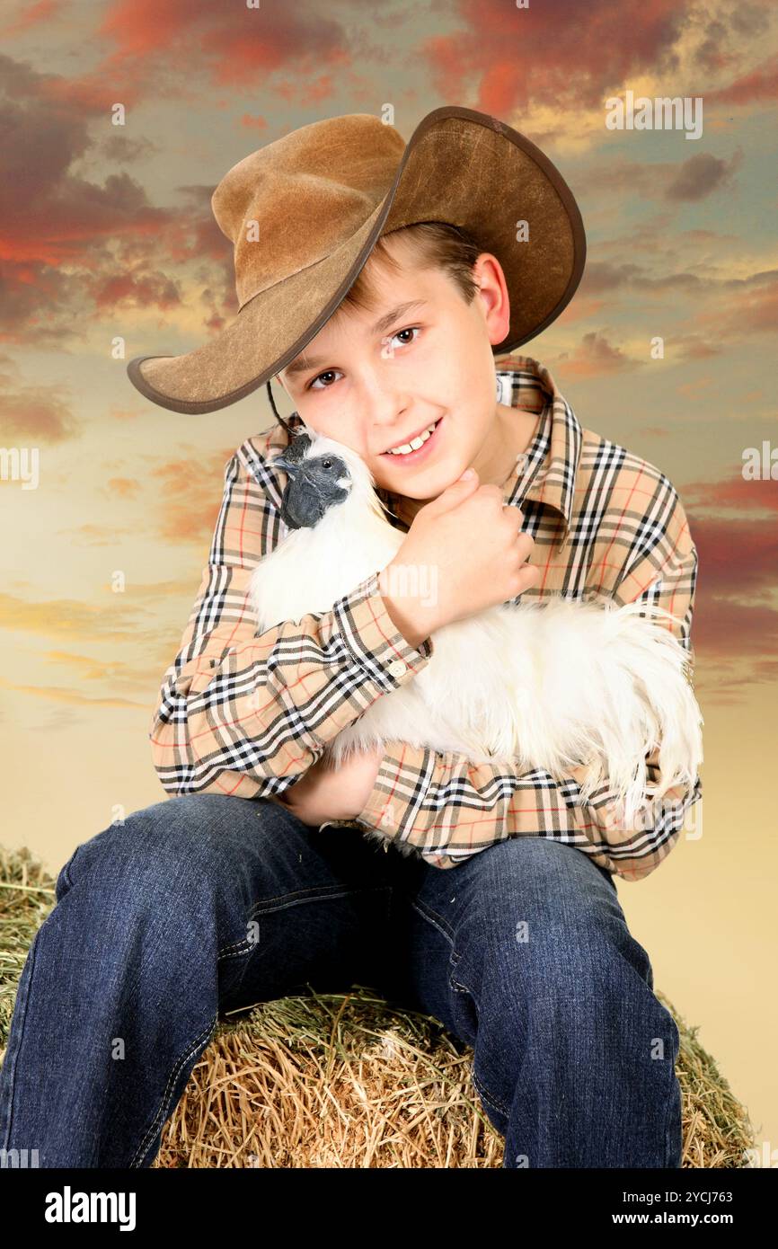 Farm boy sitting on bale of hay holding a chicken Stock Photo - Alamy