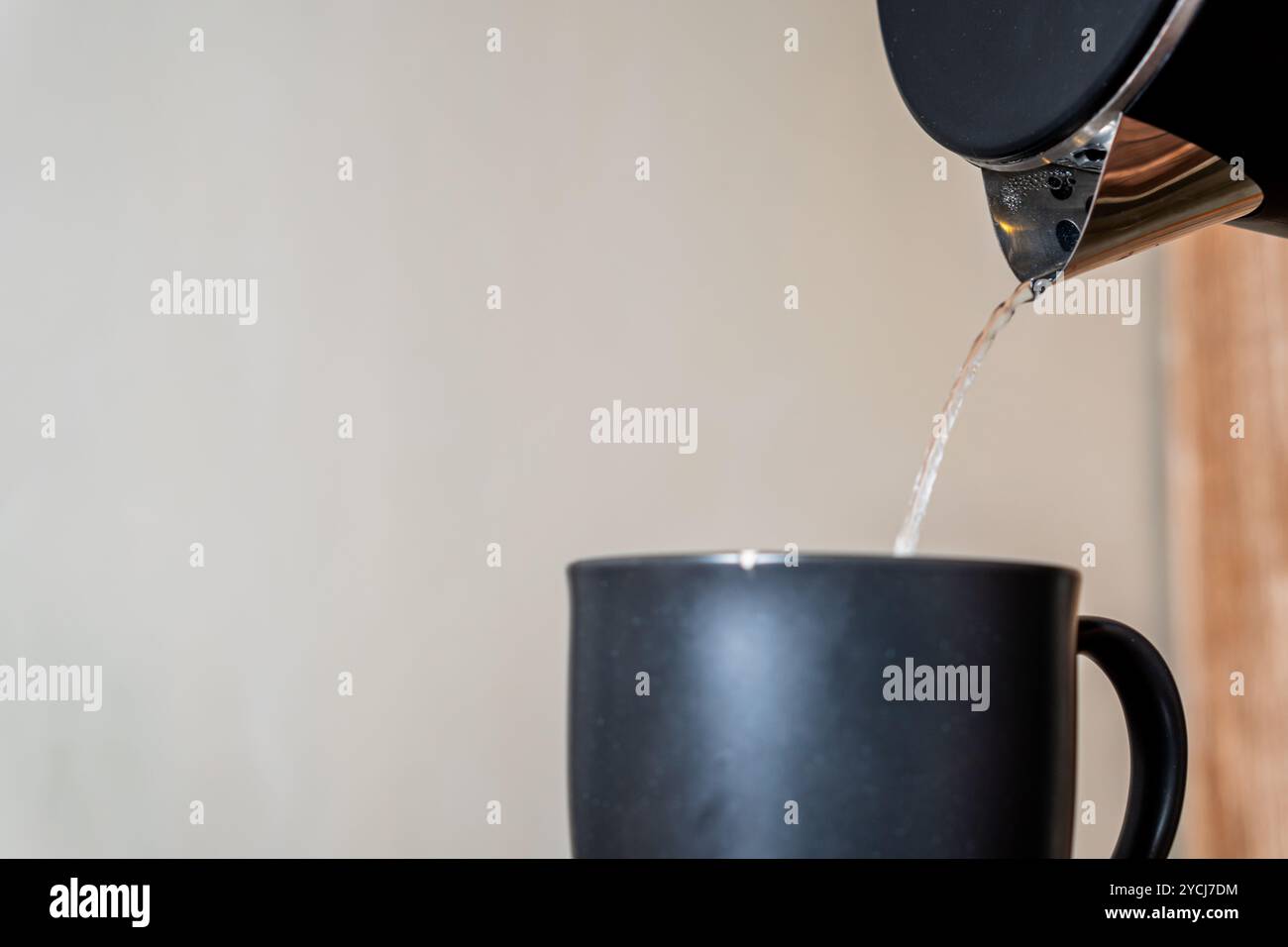 A black coffee mug placed on a woven coaster, with hot water being ...
