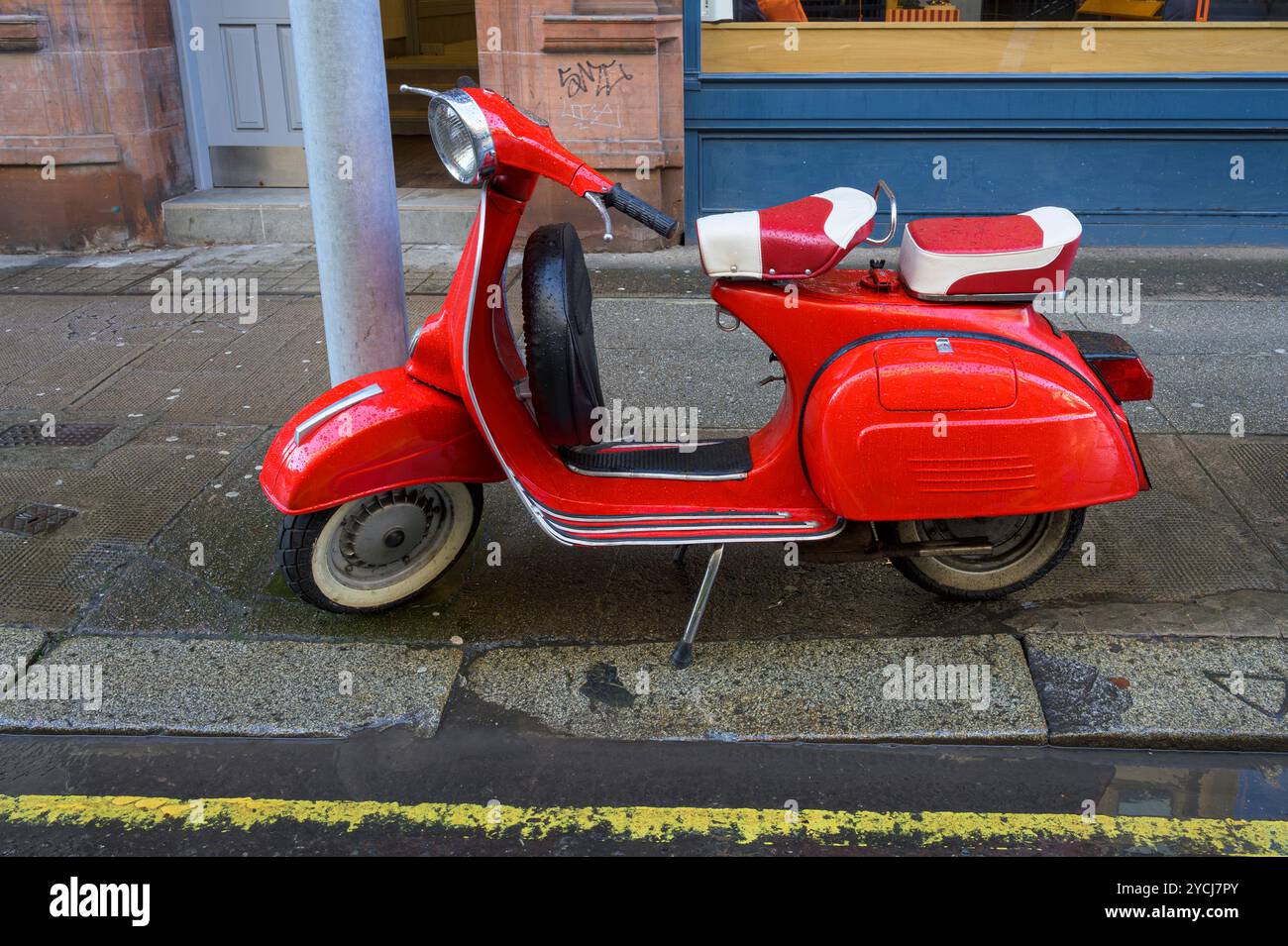 A red vintage vespa scooter parked at the roadside on a city street, UK ...