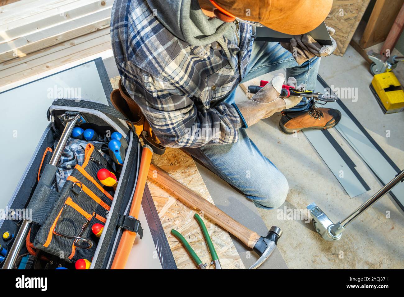A construction worker sits on the floor, focused on using tools from a ...