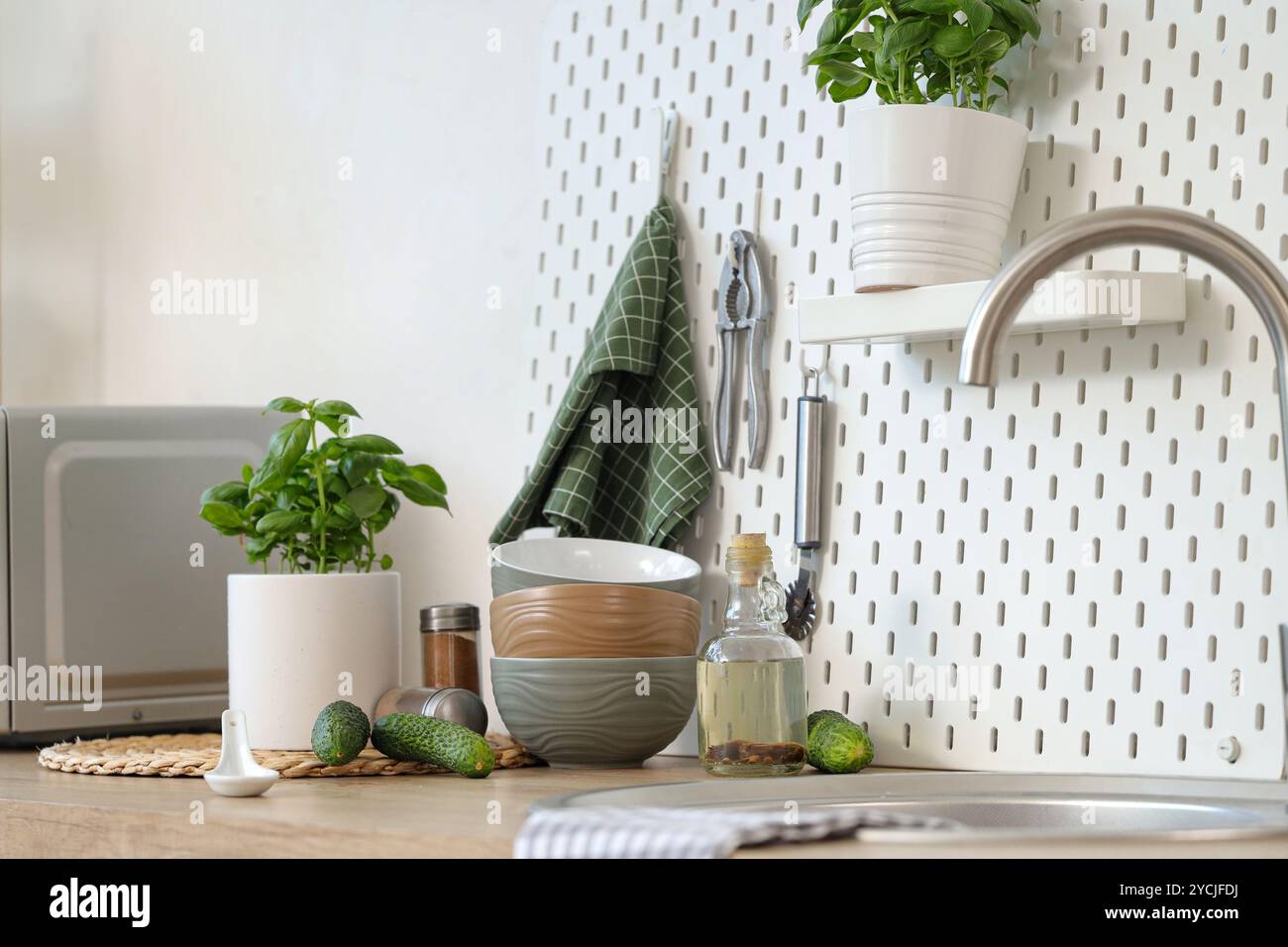 Basil plants with bowls, spices and cucumbers on table in kitchen Stock ...