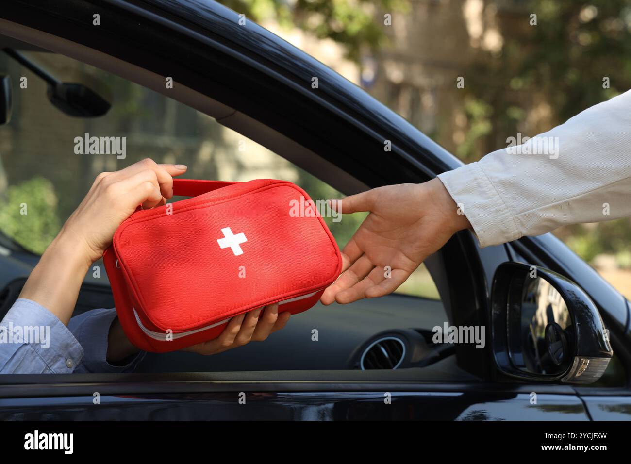 Woman on passenger seat passing first aid kit to person outside car ...