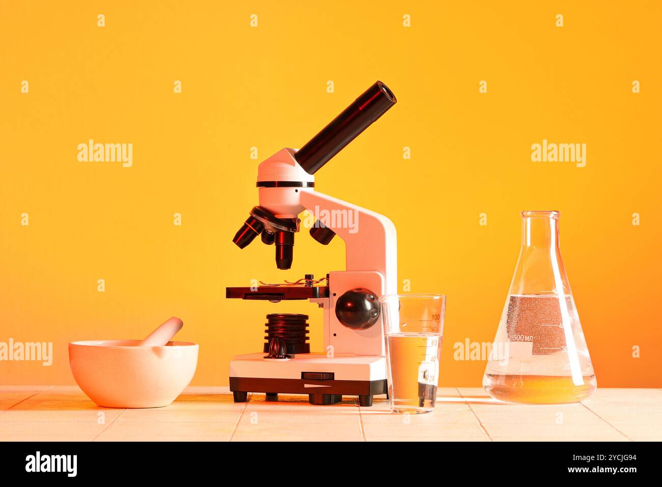 Modern microscope, mortar and laboratory glassware with liquid on white ...
