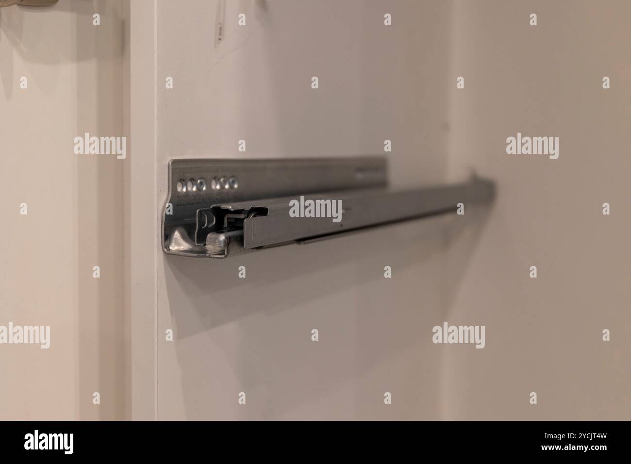 A metal drawer slide rail installed on a white cabinet wall, showcasing ...