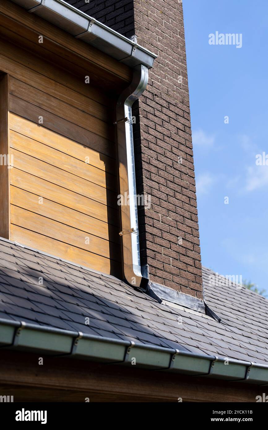 A tall, dark brick chimney stands beside a sleek metal gutter, which ...