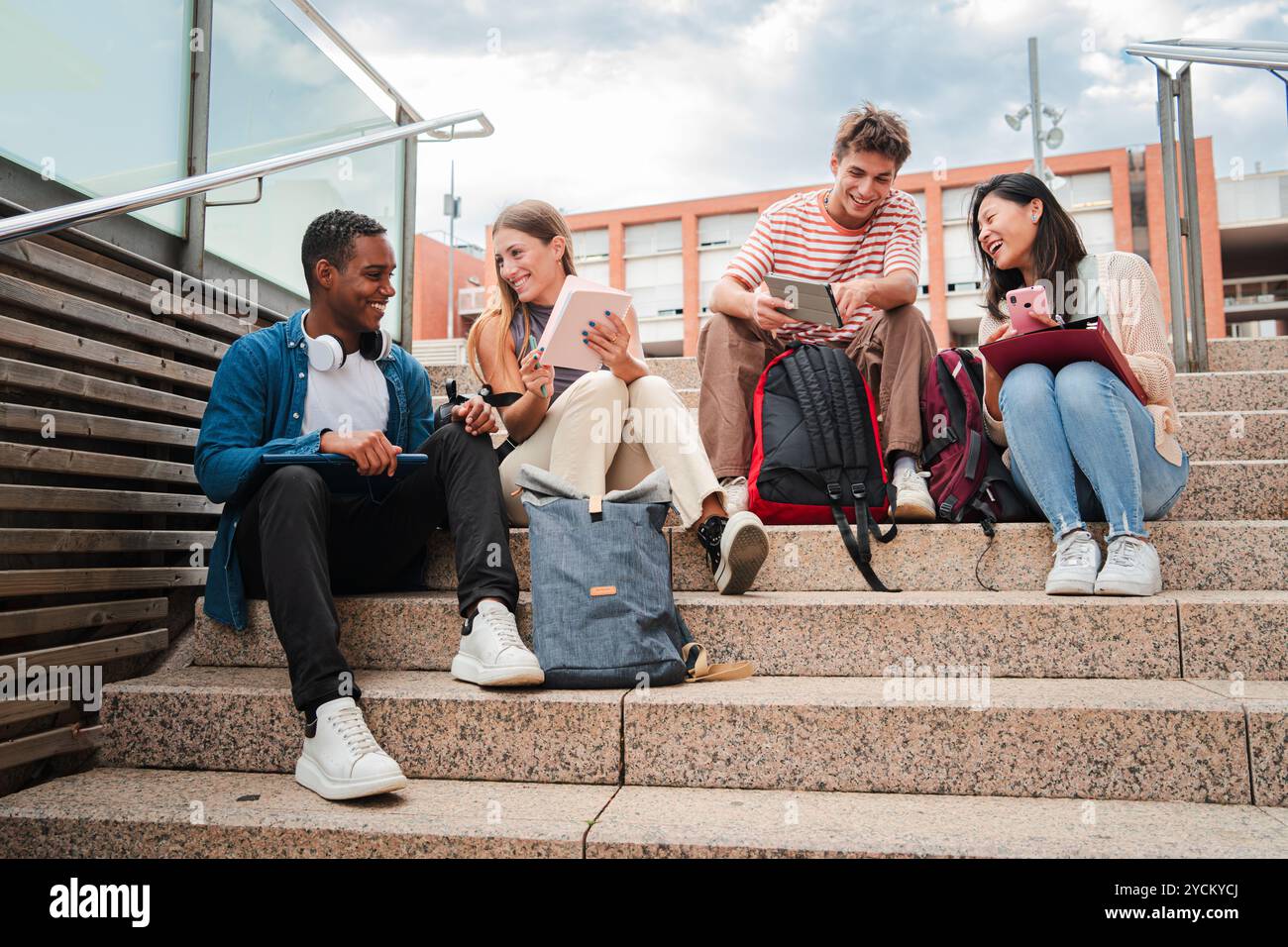 Group of diverse young students talking and smiling while sitting on ...