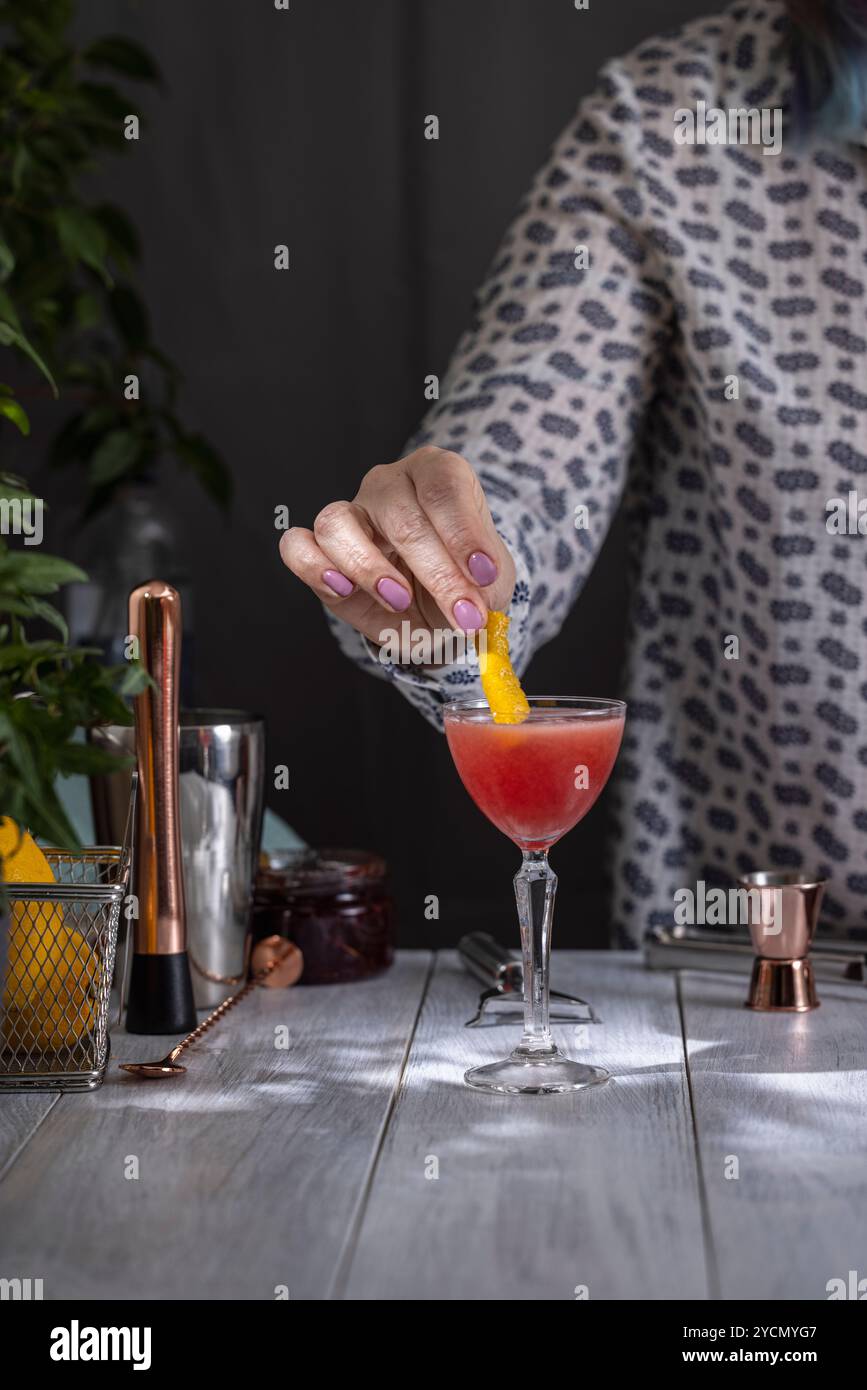 Bartender is adding a lemon zest to a red cocktail in a coupe glass on a bar counter Stock Photo ...