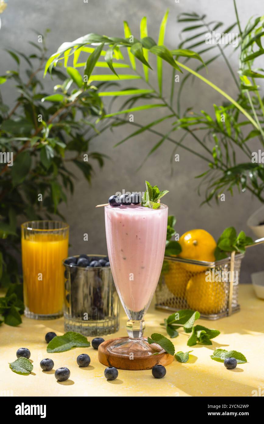 Refreshing blueberry milkshake standing on yellow counter with mint and ...
