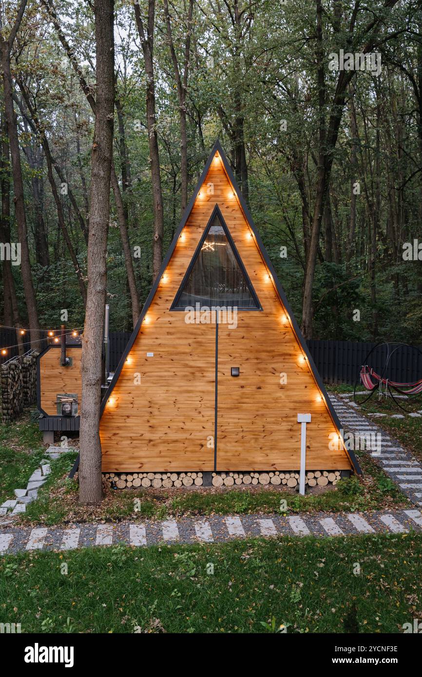 Cozy wooden A-frame cabins in forest with sunlight and outdoor seating ...