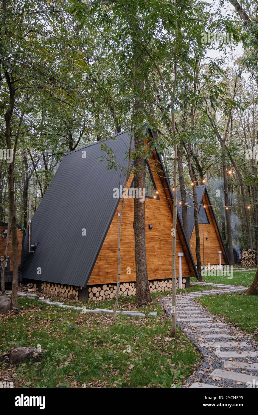 Cozy wooden A-frame cabins in forest with sunlight and outdoor seating ...