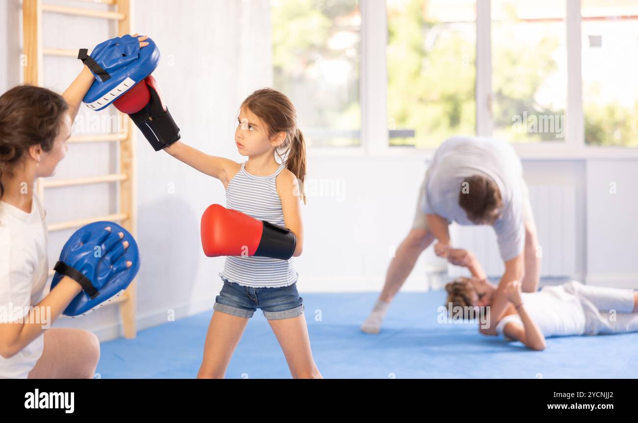 Little girl in boxing gloves learns to box from the punch mitts of her ...