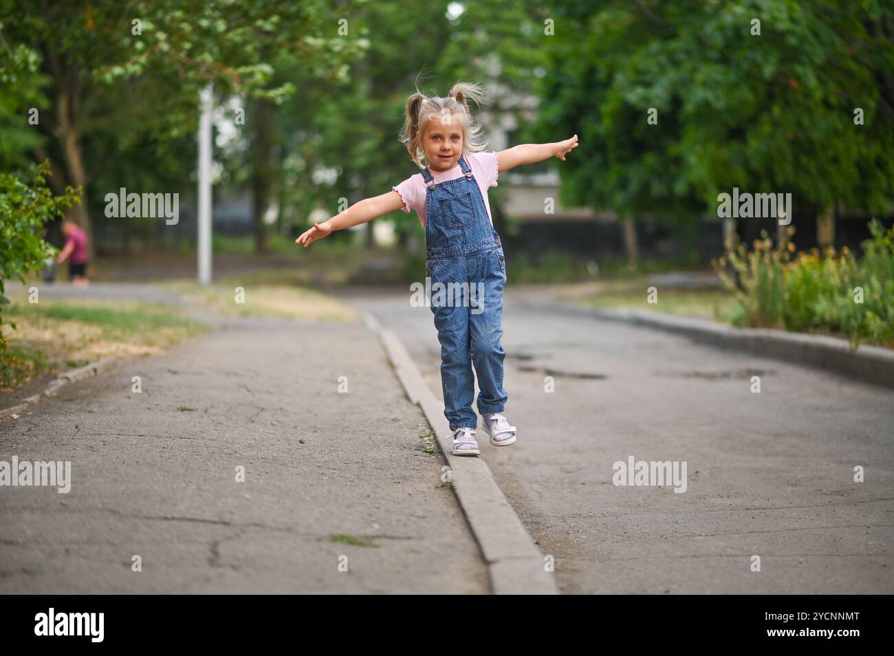 The girl walks along the sidewalk, keeping her balance, arms ...