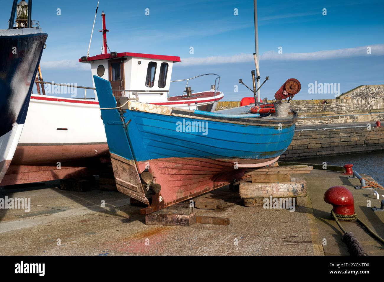 Colourful fishing boats lifted out of the water and resting on blocks ...