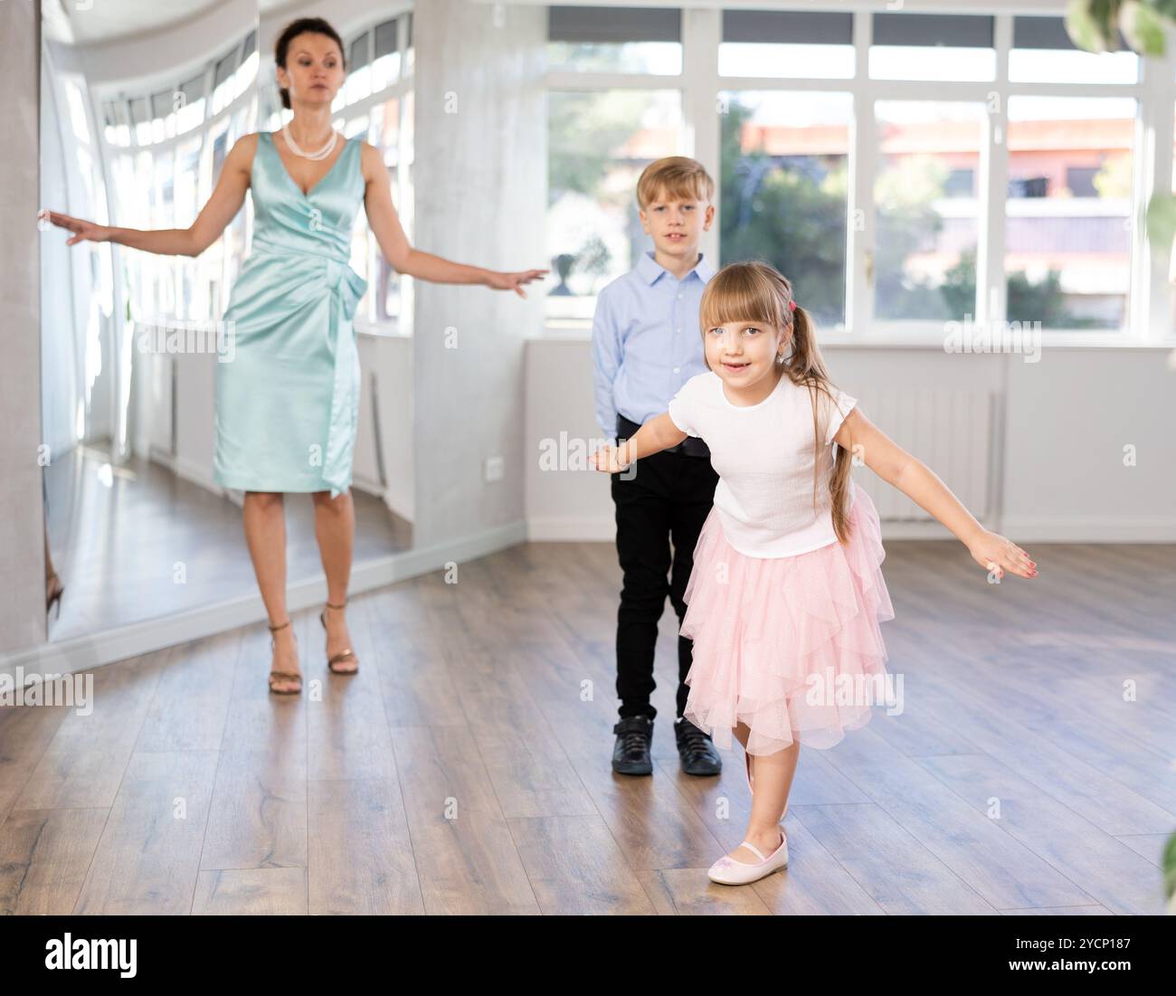 Girl rehearsing elegant curtsy with boy dance partner and female ...