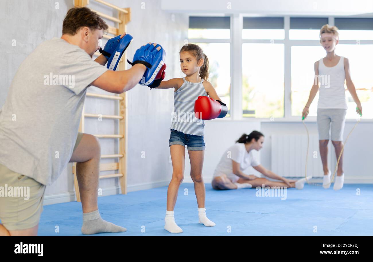 Girl with her trainer father at gym. Boy wearing boxing gloves exercise ...
