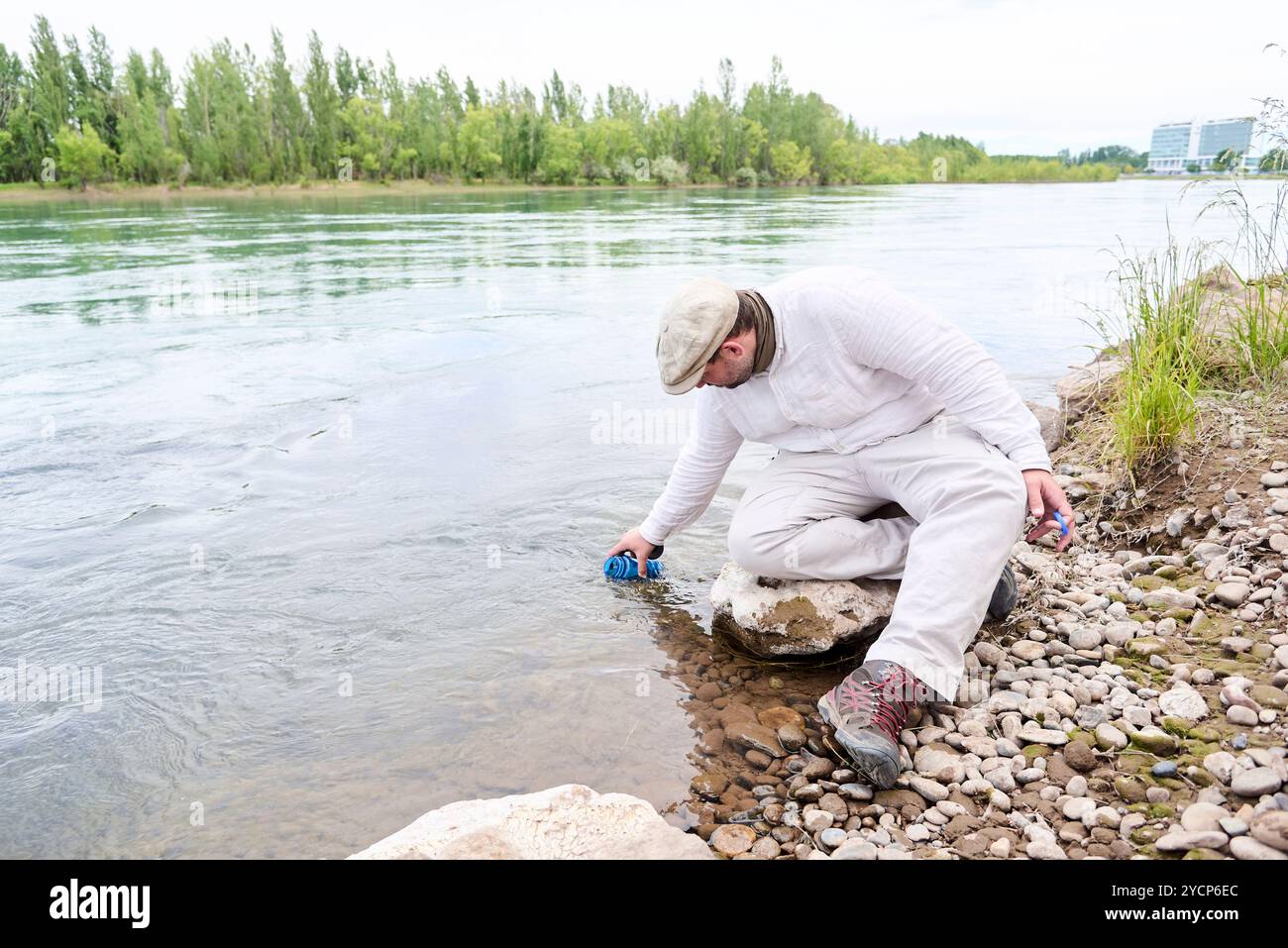 Man on the bank of a clean river collecting water in a bottle. Concepts ...
