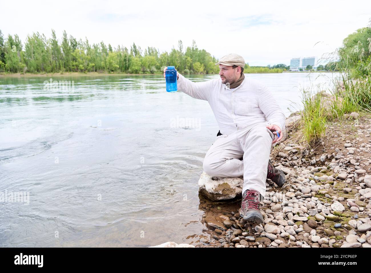 Man collecting water from a river in his bottle and looking at its ...