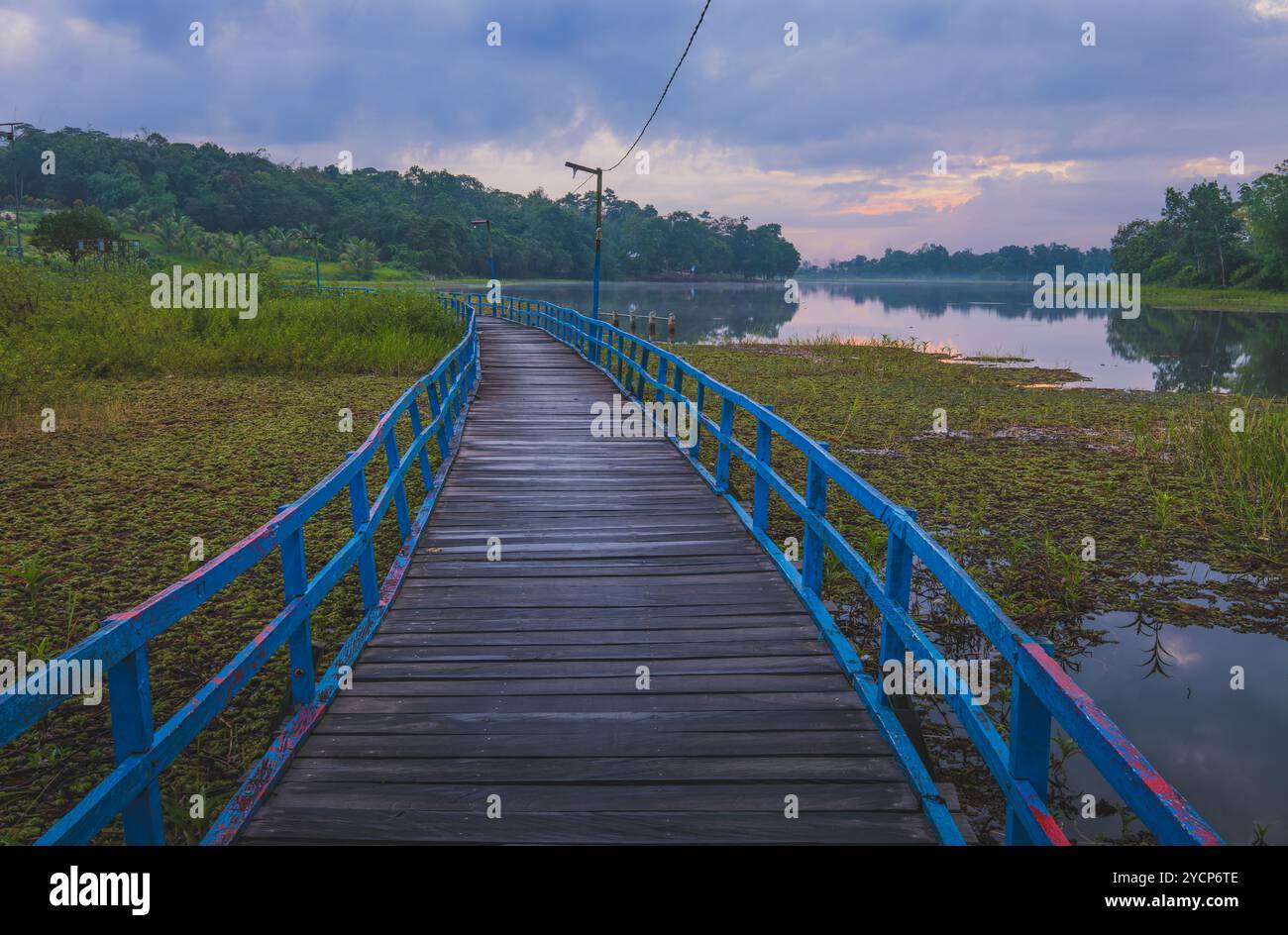 A scenic image of a long wooden bridge stretching into a calm lake. The ...
