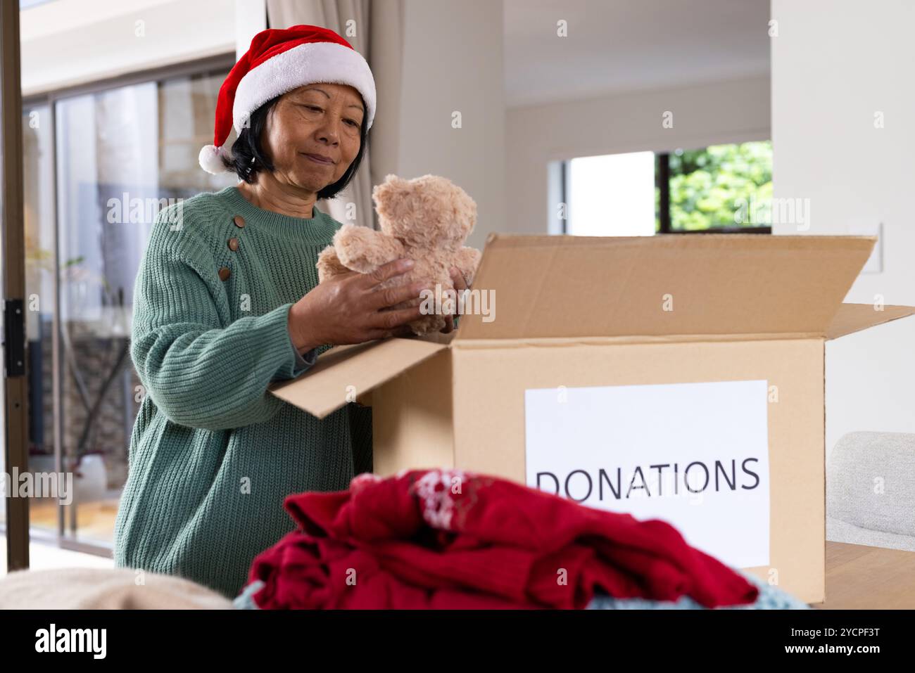 Senior asian senior woman in Santa hat packing teddy bear into donation ...