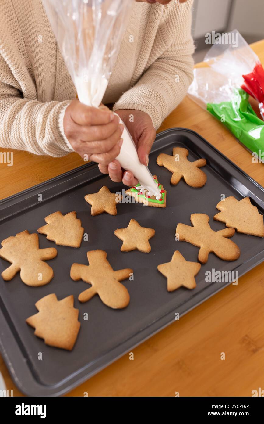 Decorating christmas cookies at home, asian senior woman adding icing ...