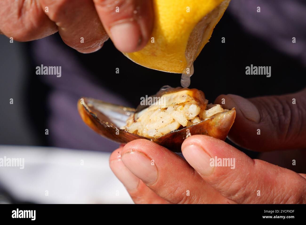 A hand squeezing fresh lemon juice onto a clam shell to enhance the ...