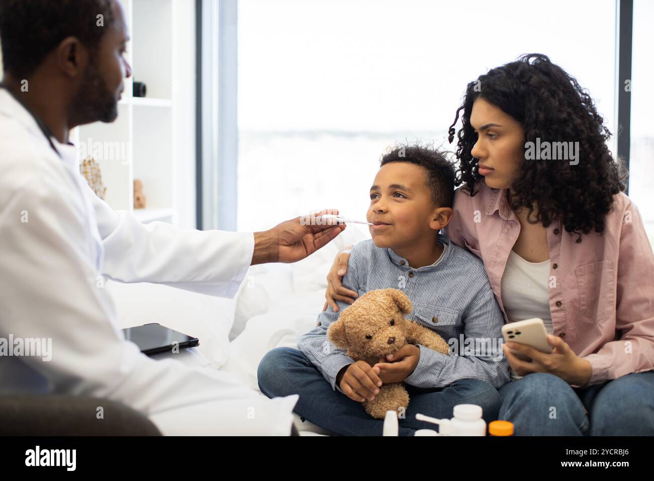 Male doctor measuring temperature of young boy with mother present ...