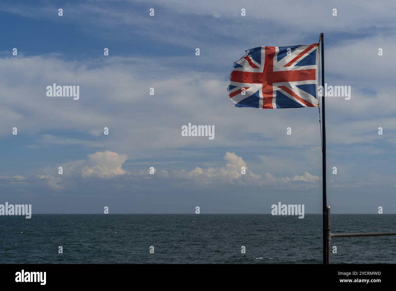 A tattered and torn Union Jack flag in a stiff wind with blue ocean and ...