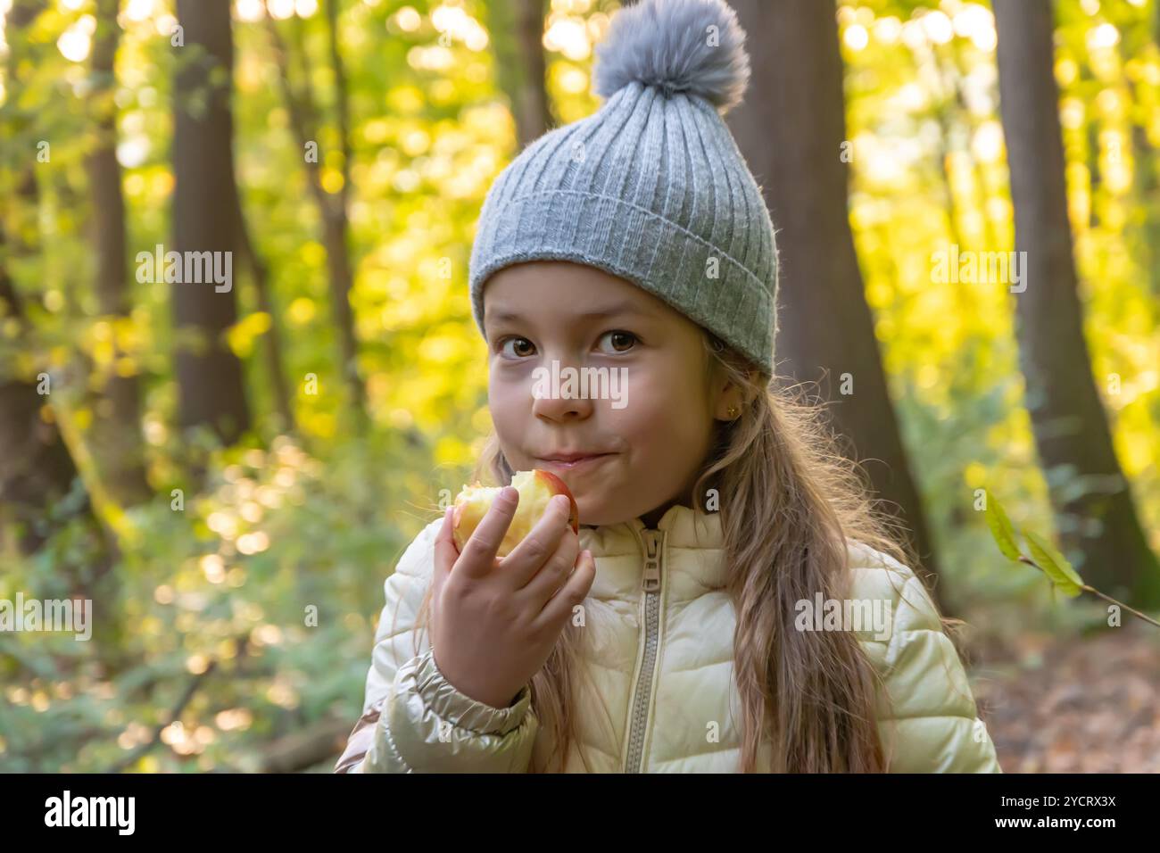 A girl eats a fresh apple while walking through a sunlit autumn forest ...