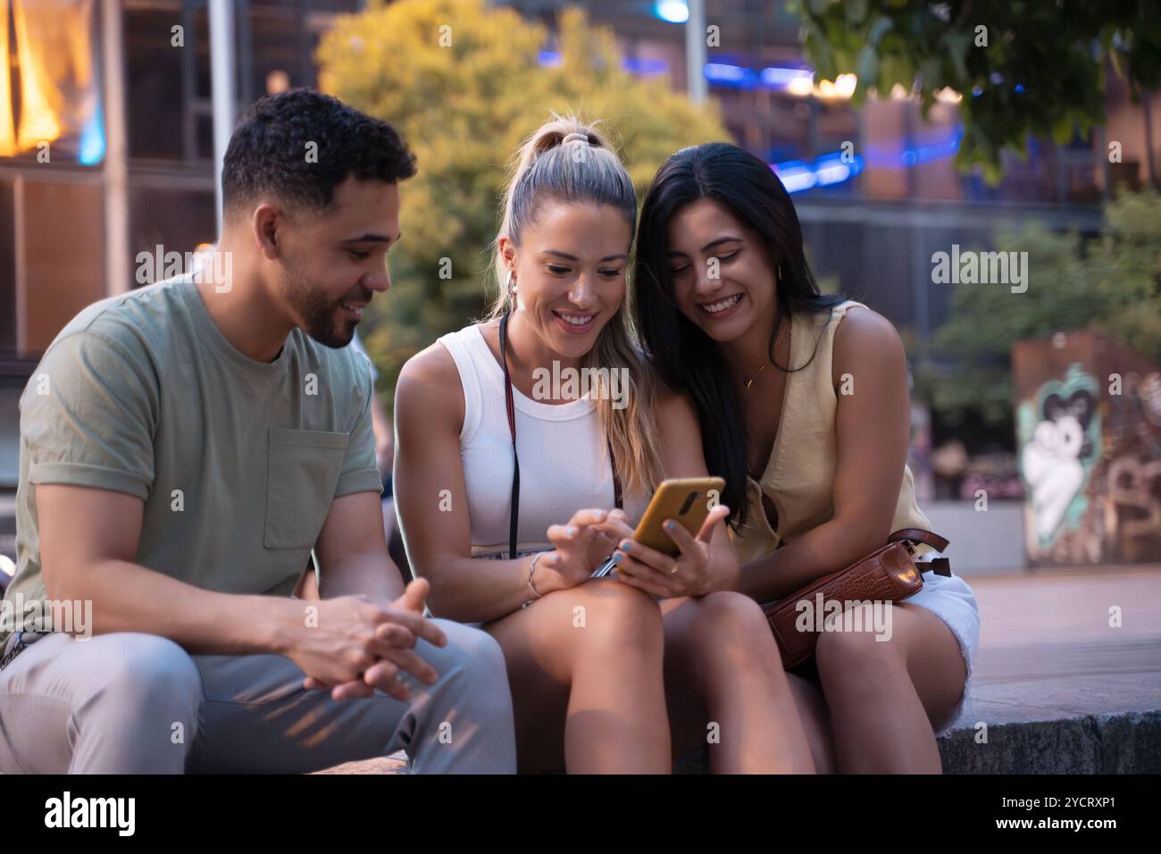Group of friends are sitting on a bench in the city at night, using a ...