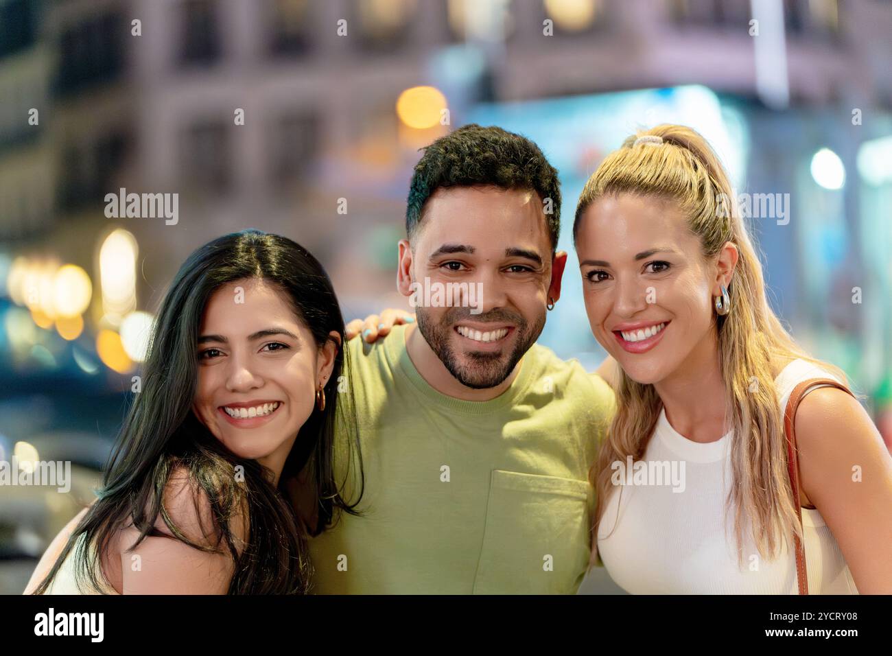 Three friends are standing together in the city at night, with their ...