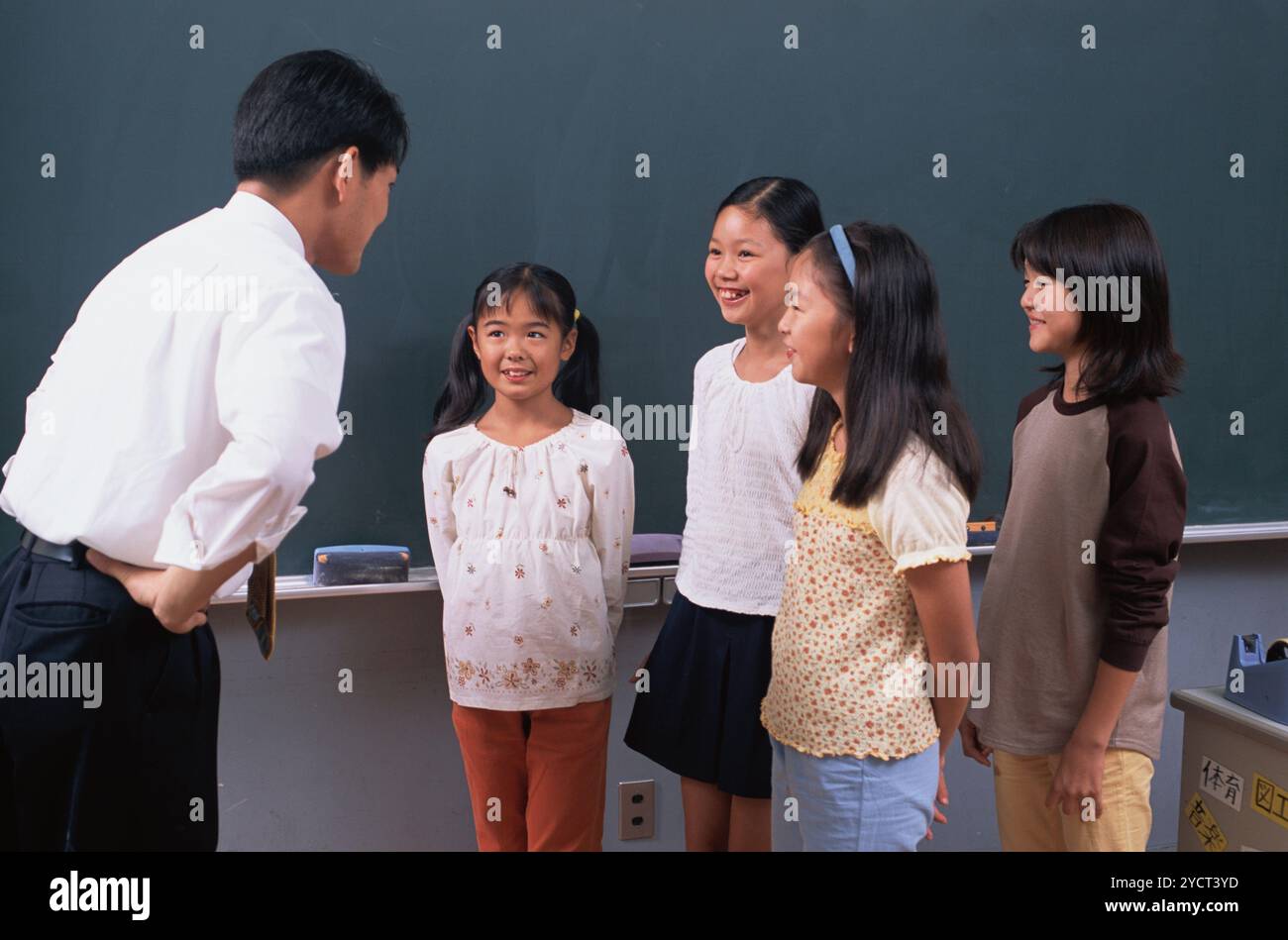 Four primary school girls and a male teacher in front of the blackboard ...