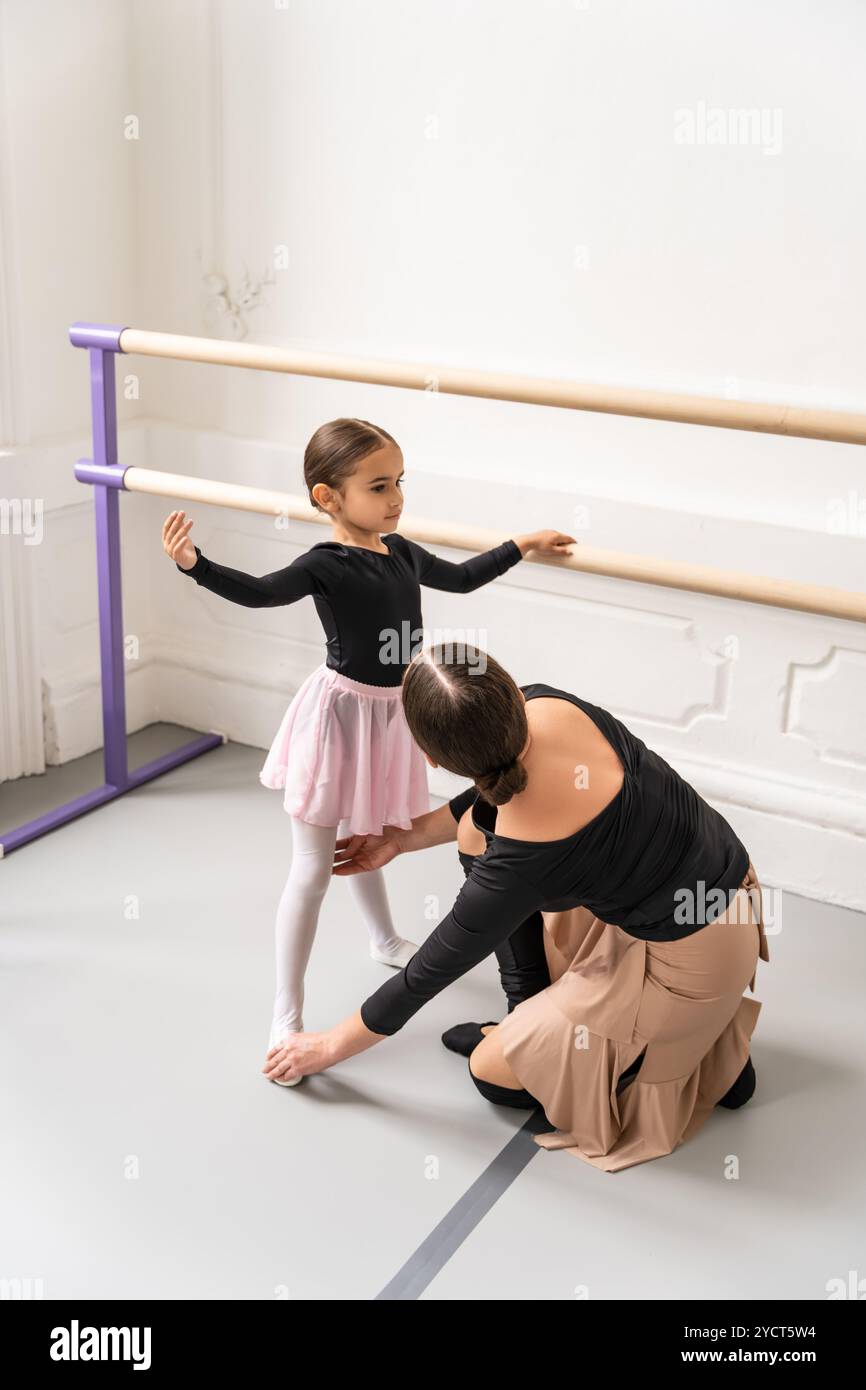 Cute little girl learning ballet from her experienced trainer in studio ...