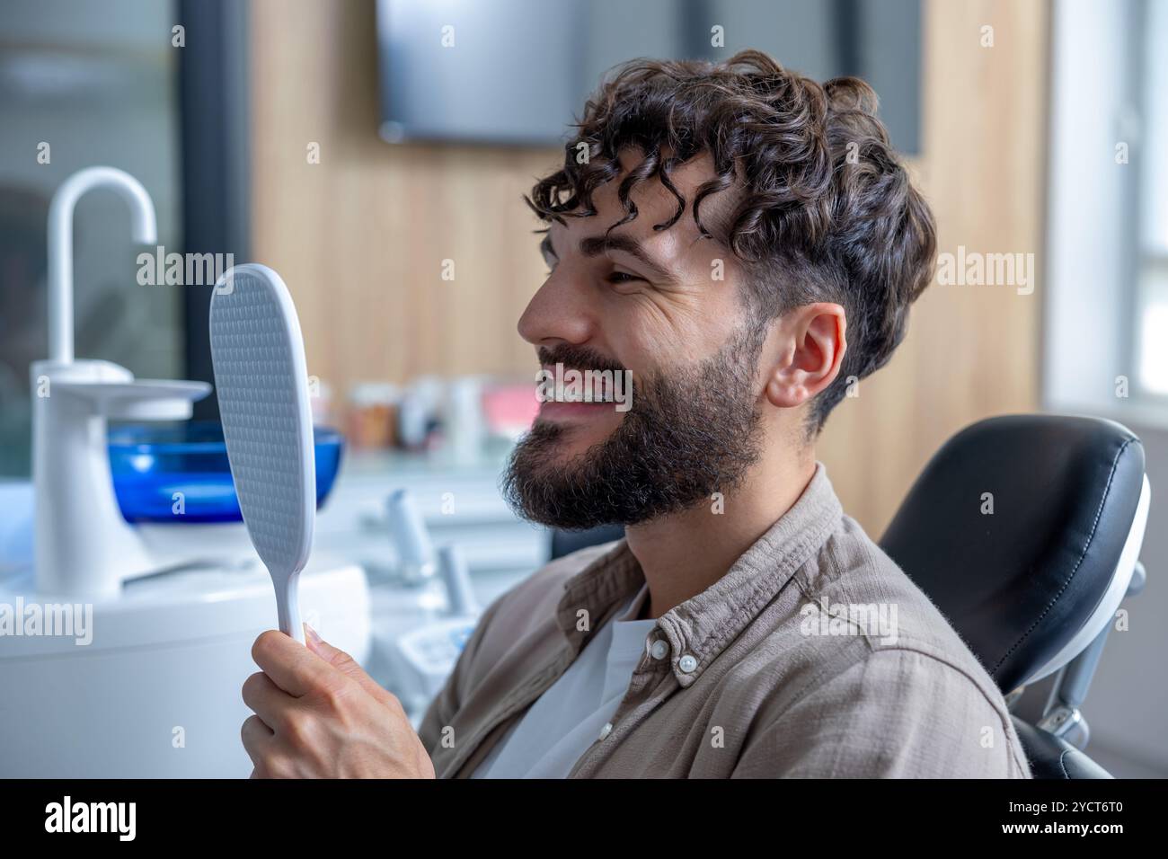 Bearded patient receiving dental treatment in clinic using mirror to ...