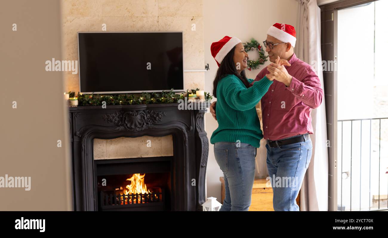 Christmas time, dancing by fireplace, senior multiracial couple in ...