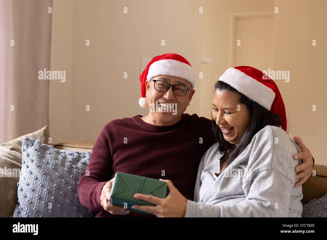 Christmas time, senior multiracial couple wearing santa hats exchanging ...