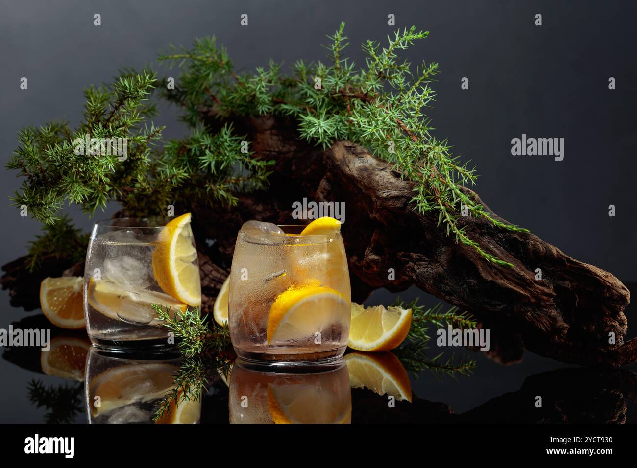 Cocktail gin-tonic with ice and lemon on a black reflective background ...