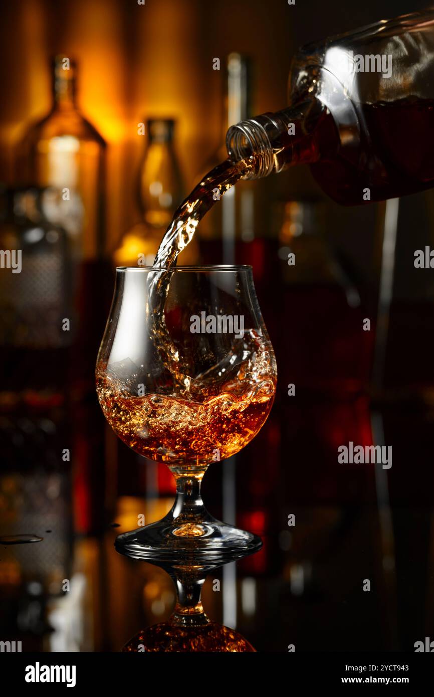 Pouring brandy from a bottle into a glass. Snifter of brandy on a black ...