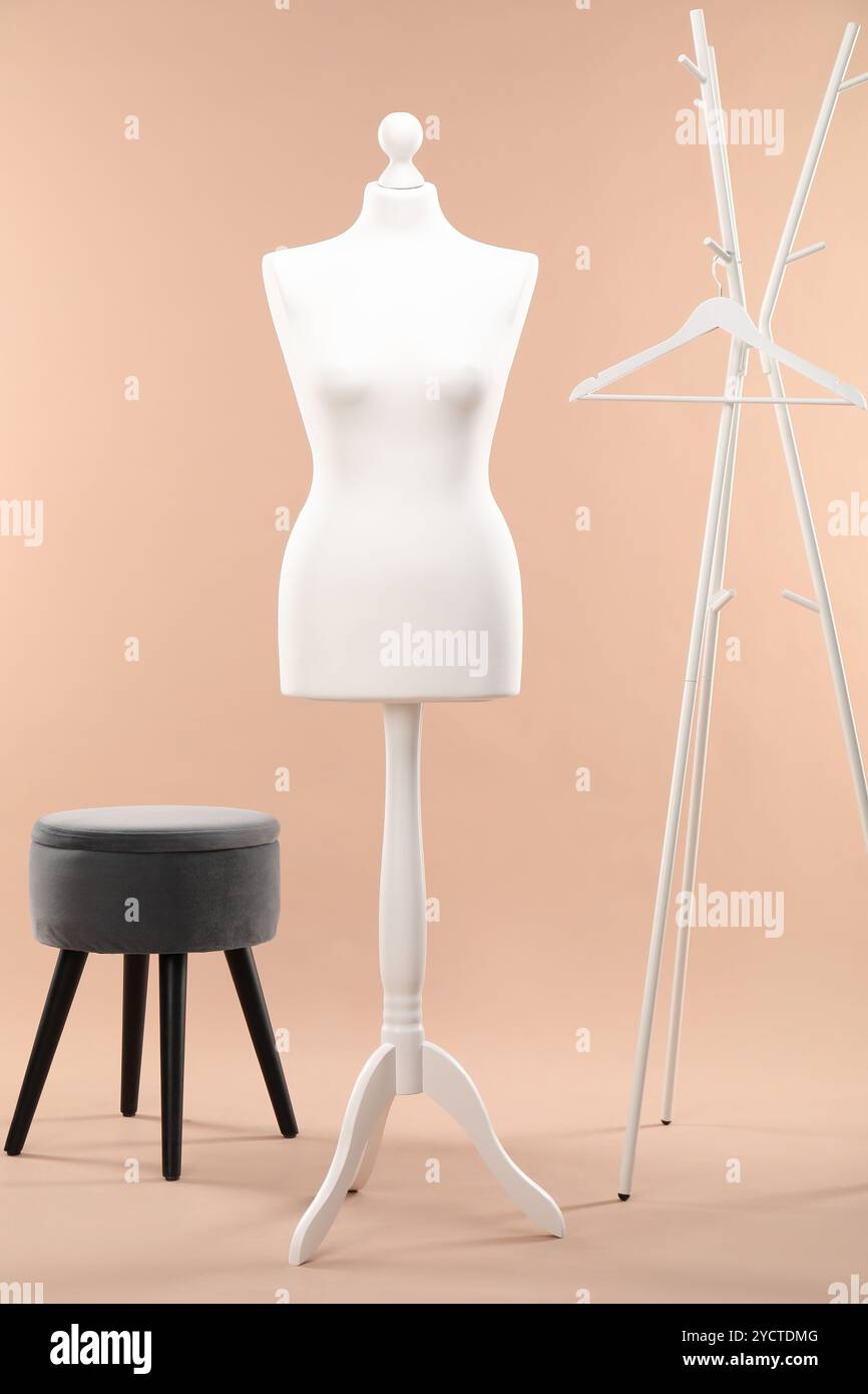 One female mannequin, rack, hanger and ottoman on beige background ...