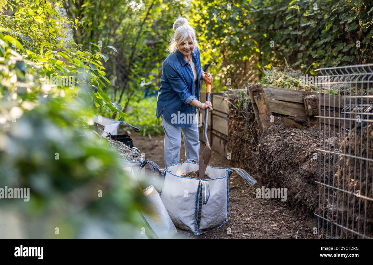 Senior woman shoveling compost heap in her garden Stock Photo - Alamy