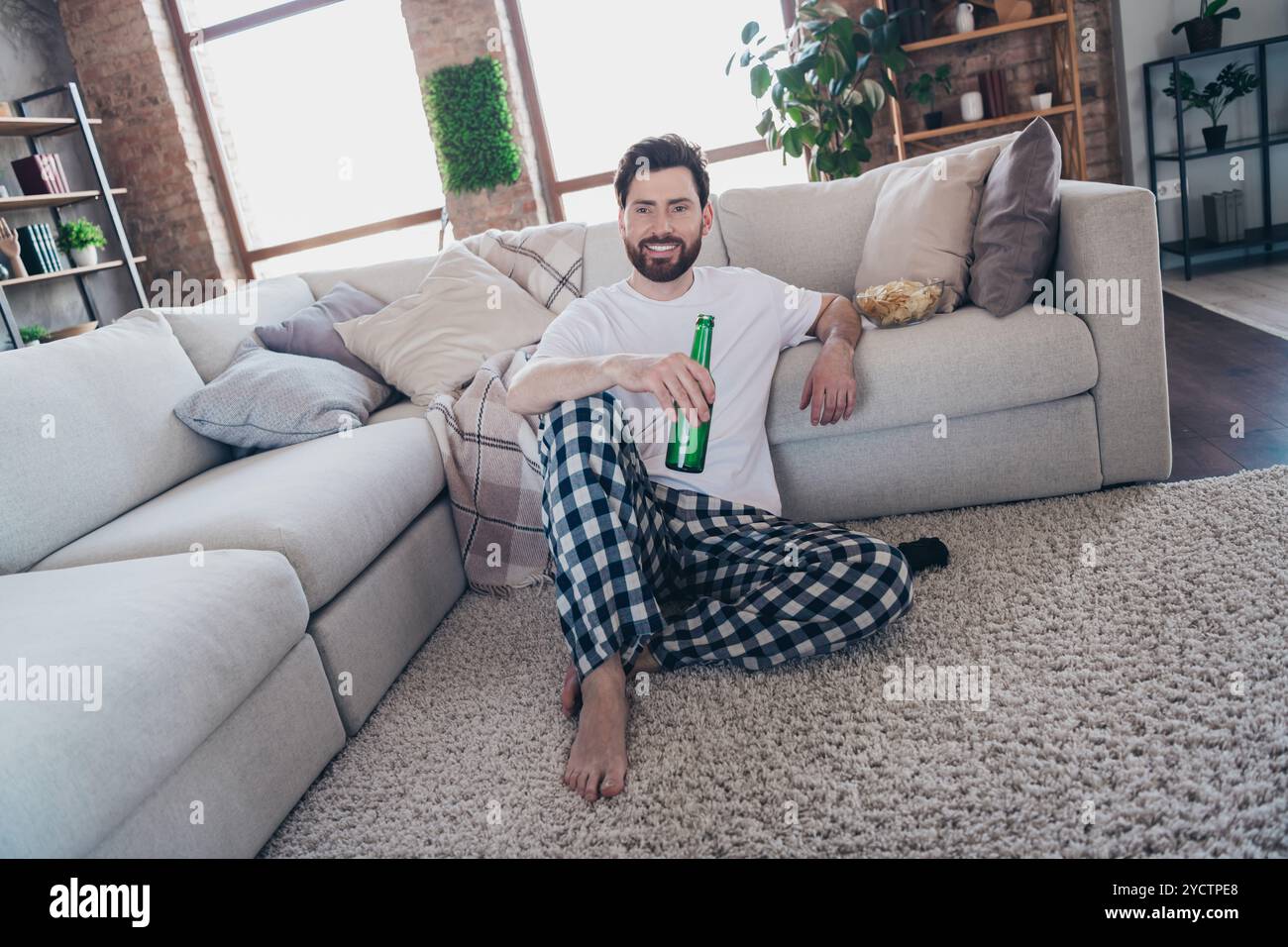 Photo of cheerful attractive man wearing nightwear sitting on floor ...