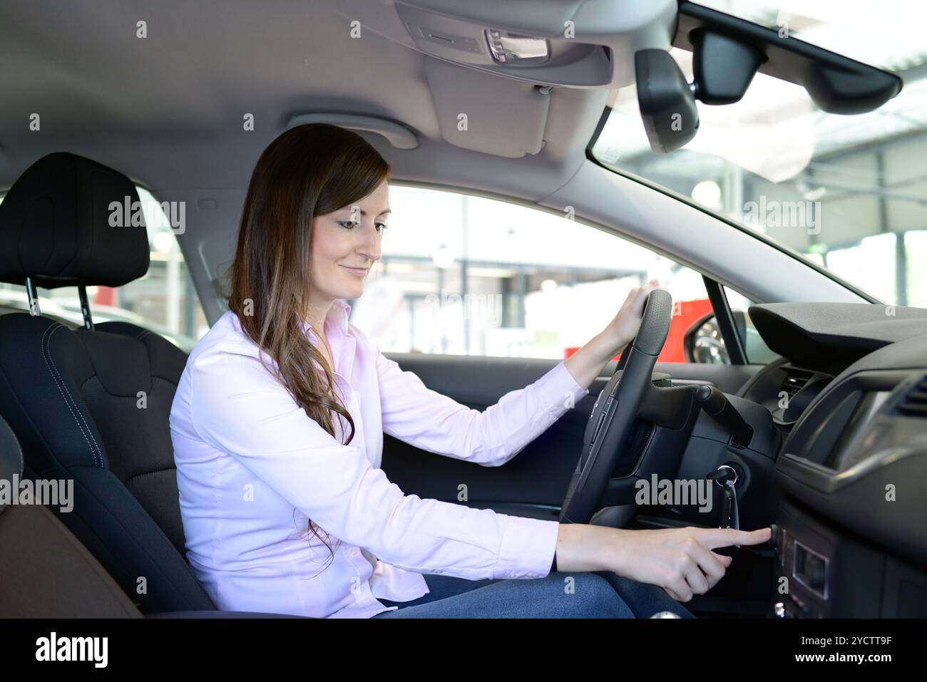 young woman sits in a new car and tests the radio - car dealership with ...