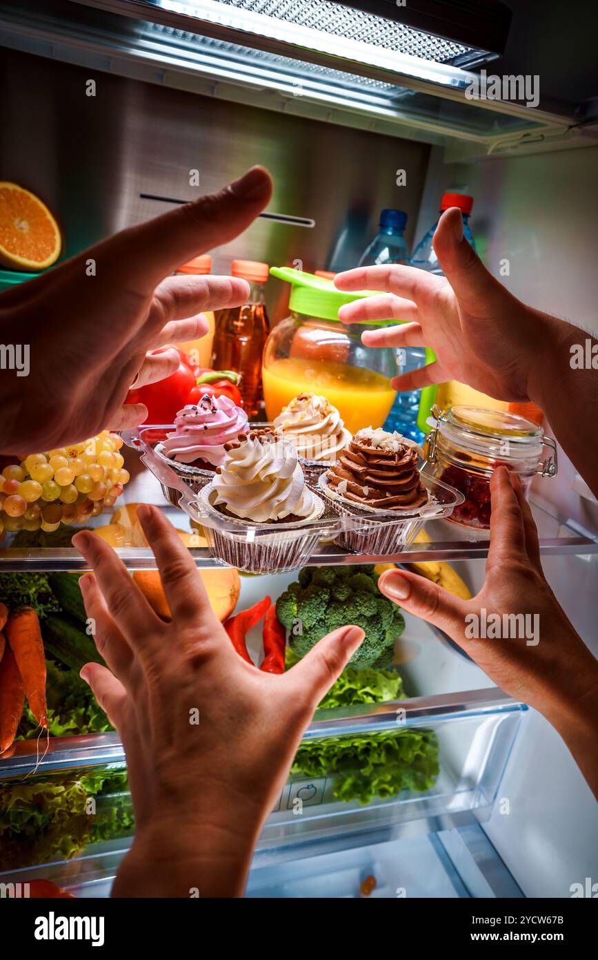 Human hands reaching for sweet cake at night in the open refrigerator ...