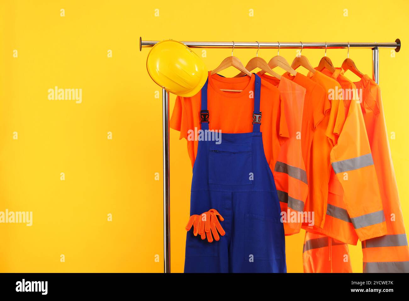 Workers' uniforms on clothing rack against yellow background. Space for ...
