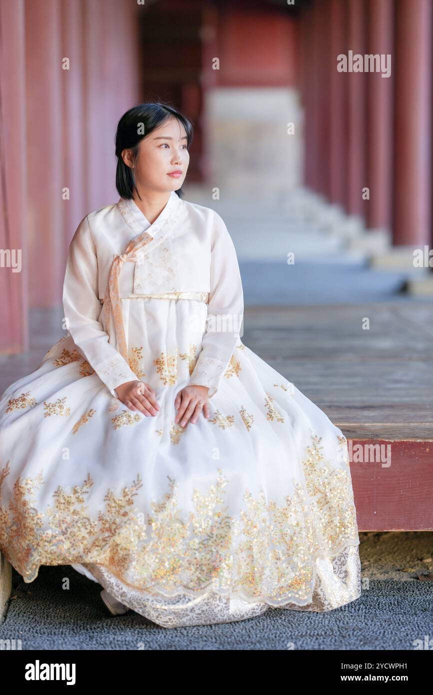 A Korean woman in her 20s wearing a white hanbok sits dignifiedly in a ...