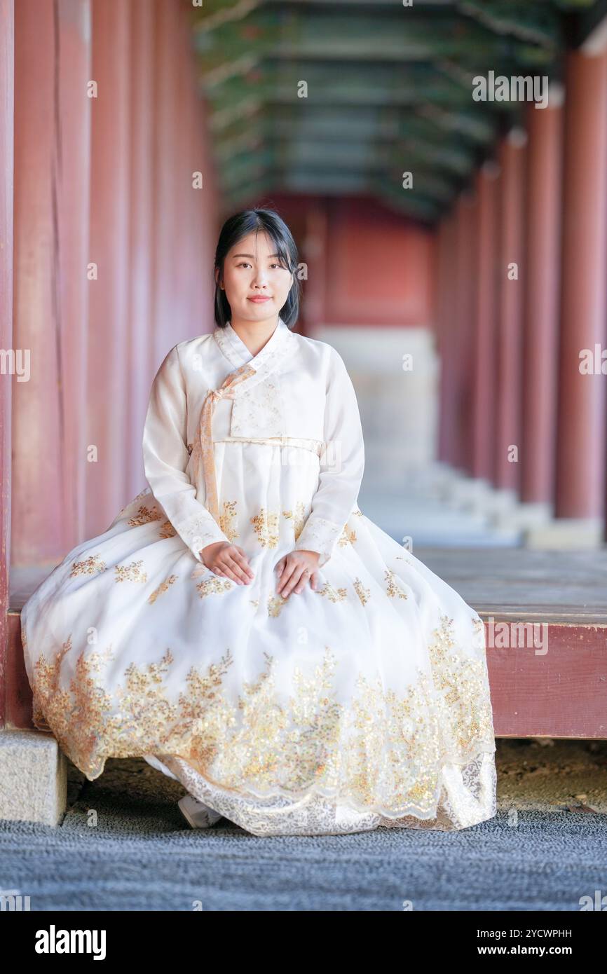 A Korean woman in her 20s wearing a white hanbok sits dignifiedly in a ...