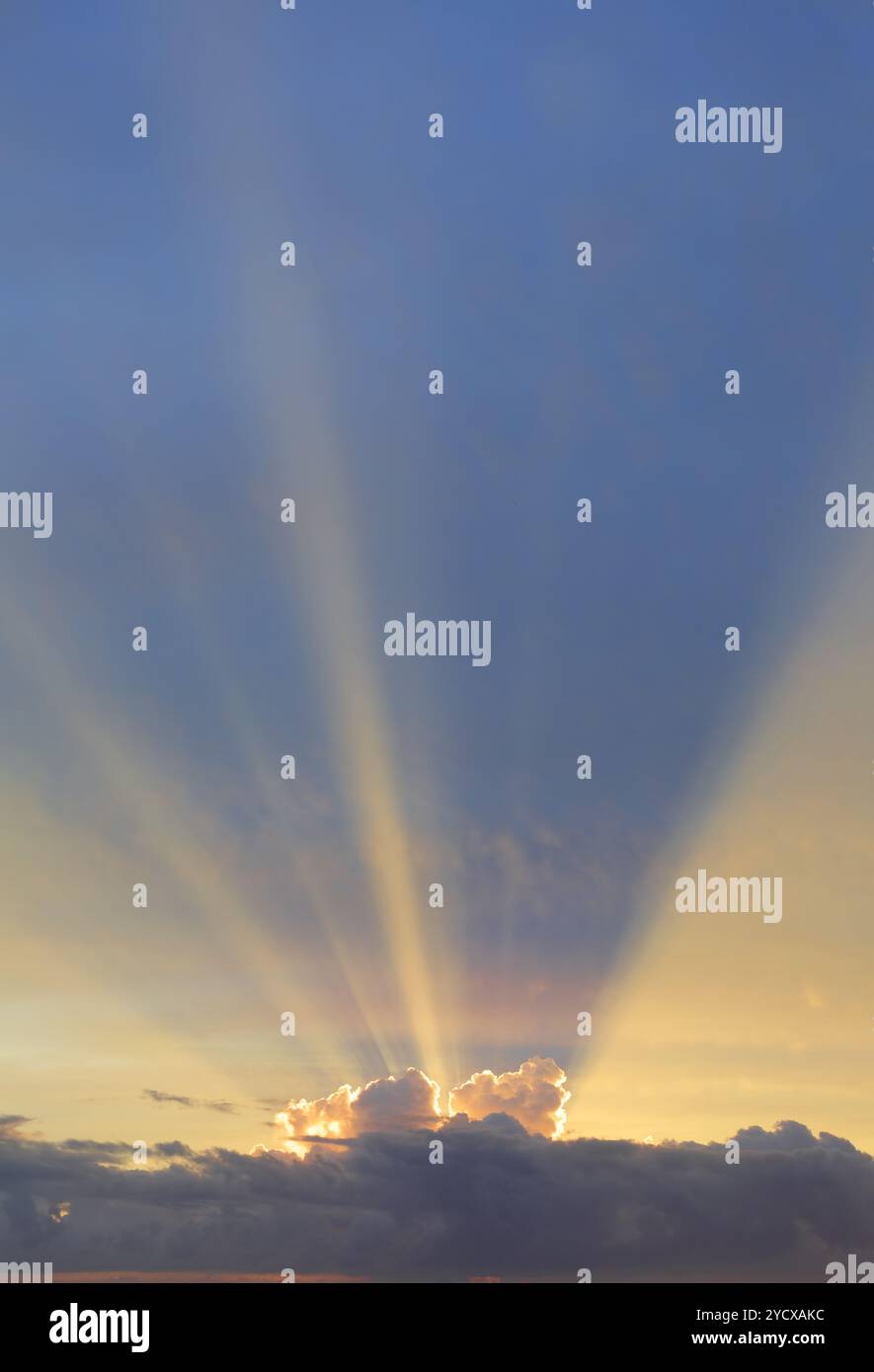 Vertical sky with sun rays bursting forth from behind clouds edged with ...